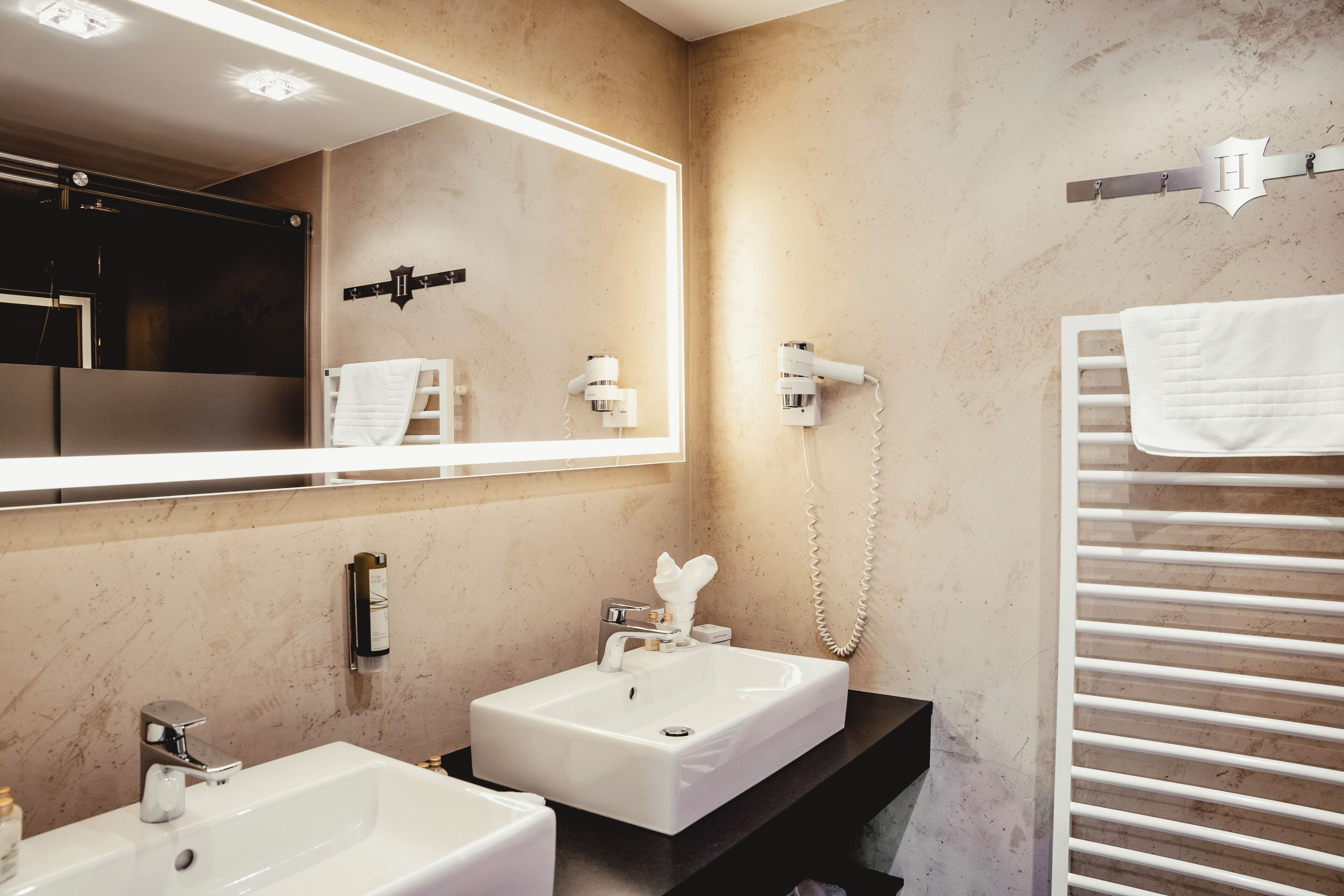Uma casa de banho moderna com duas pias, um espelho grande e um porta-toalhas.