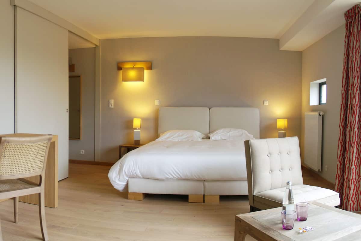 Quarto de hotel com cama, escrivaninha, cadeira, mesa pequena e mesa de cabeceira com duas luminárias.