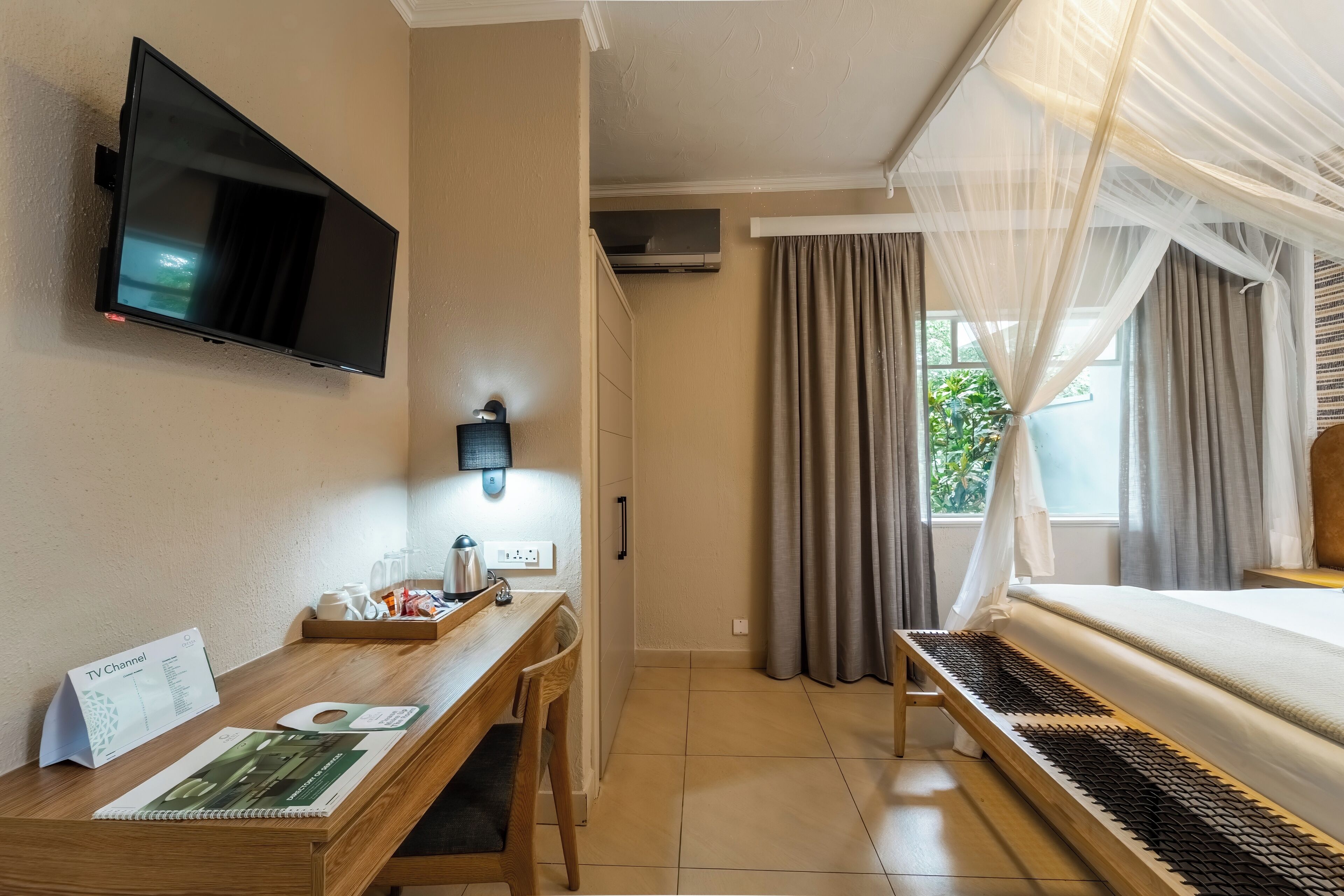 Quarto de hotel com cama, televisão, secretária e janela com cortinas.