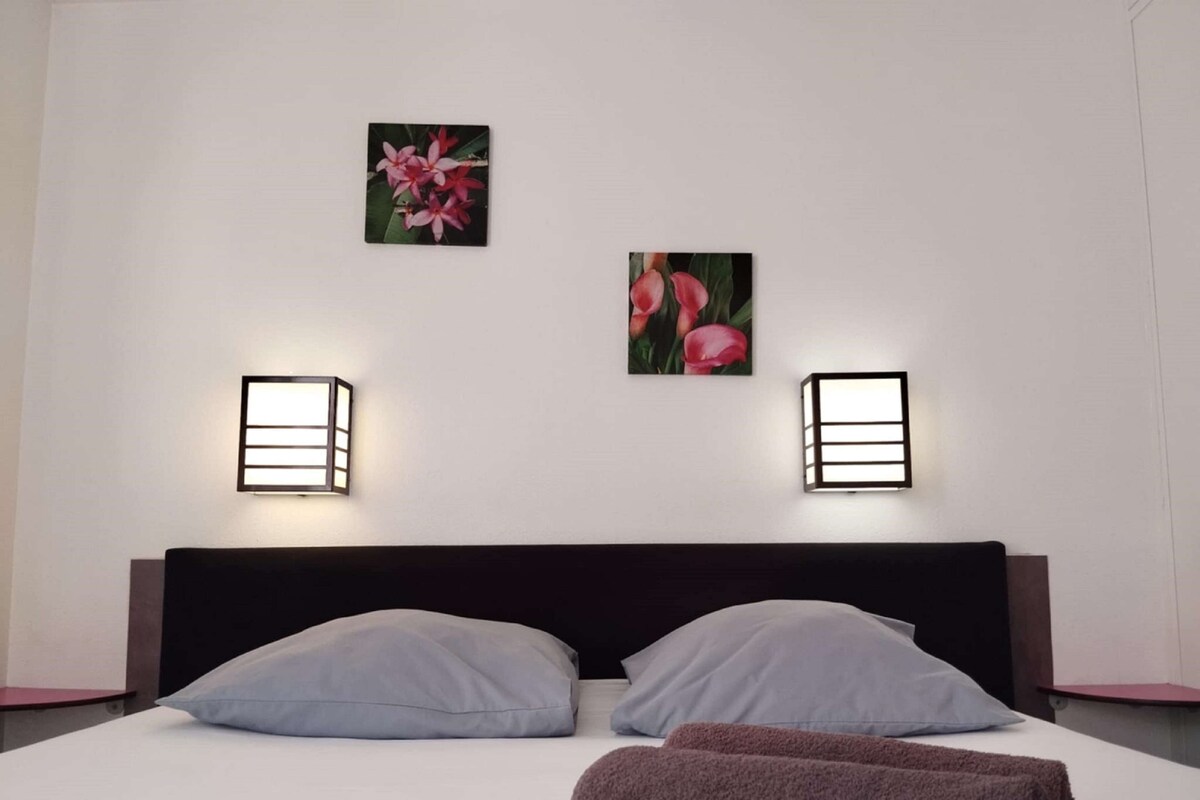 Quarto com cama, duas luzes fixadas na parede e duas imagens florais emolduradas.