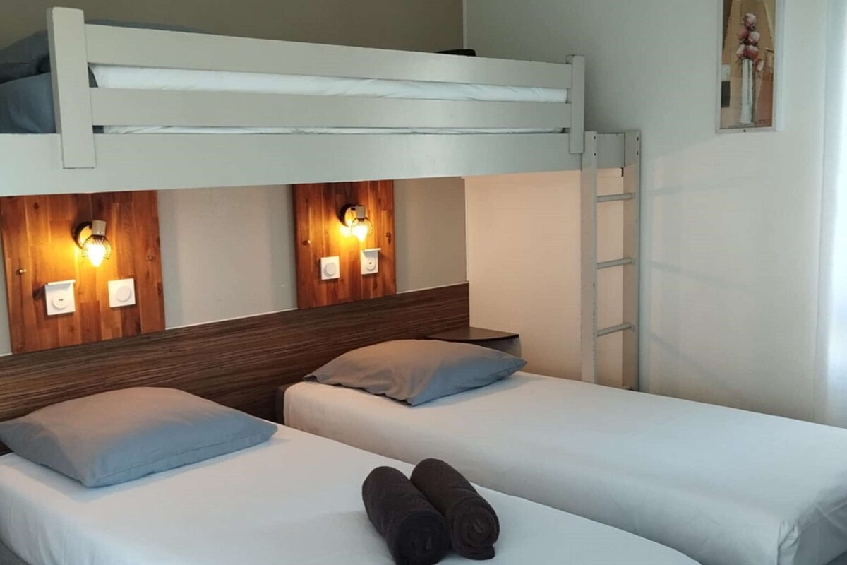Quarto com duas camas de solteiro e um beliche, acessível por uma escada.