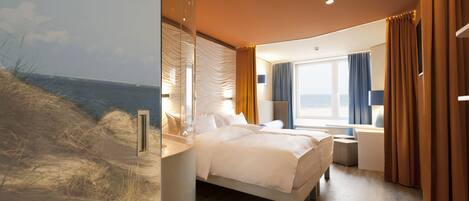Quarto de hotel moderno com uma cama grande, janela com cortinas e vista para o mar.