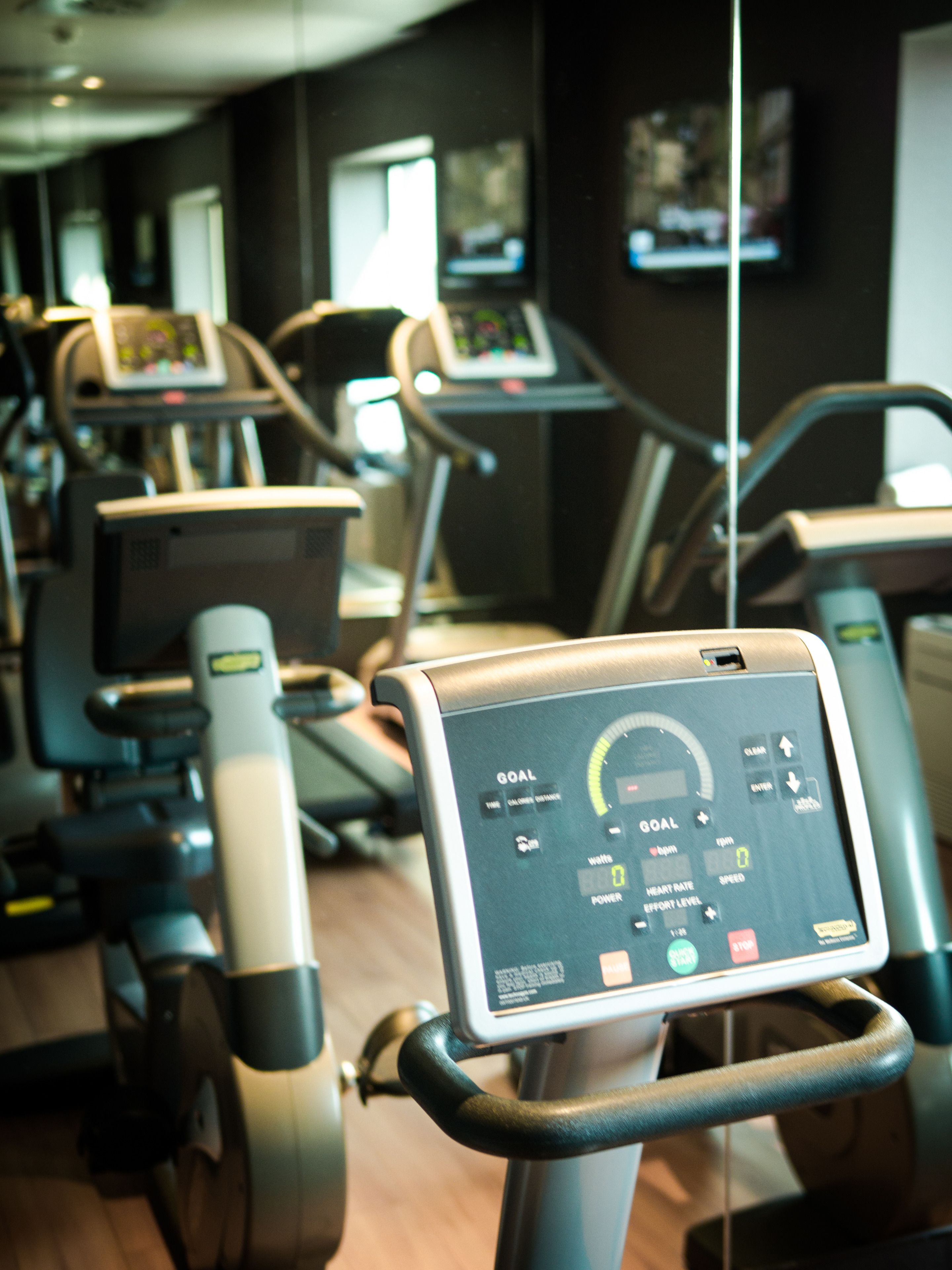 Uma academia com equipamentos de ginástica, incluindo esteiras e bicicletas ergométricas, e um visor digital em uma das máquinas.