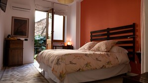 Quarto com cama, mesa de cabeceira, luminária e janela com vista para o verde.
