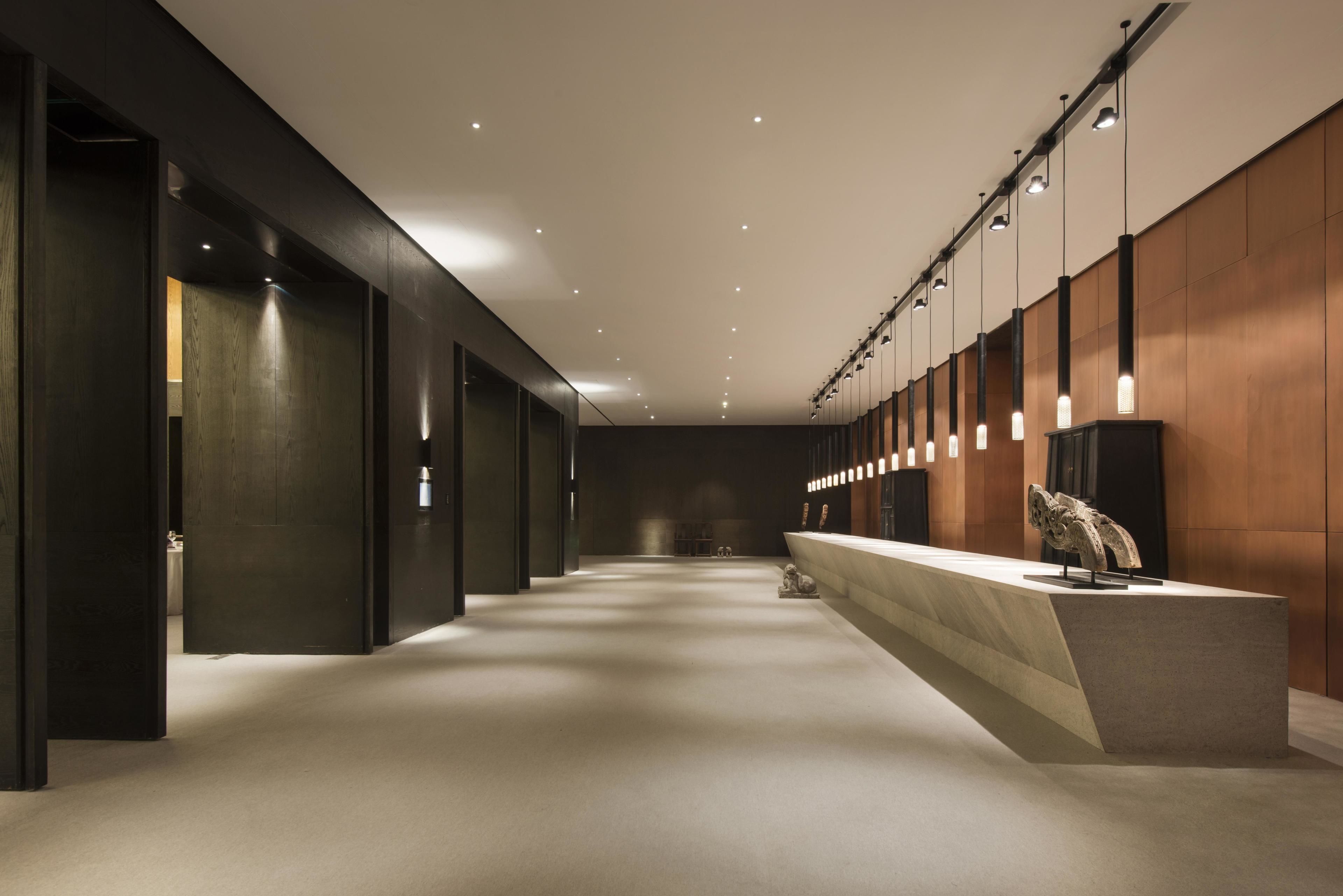 Um hall de hotel moderno com um balcão de recepção alongado, painéis de madeira escura e iluminação embutida.
