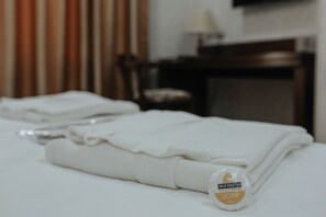 Toalhas brancas dobradas e uma garrafa de sabonete em uma cama de quarto de hotel.