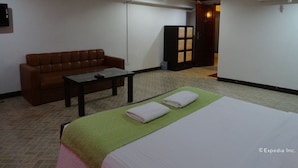 Quarto de hotel com cama, sofá de couro marrom, mesinha e guarda-roupa.