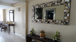 Uma área de recepção com um espelho grande, um banco com objetos decorativos e uma escada ao fundo.