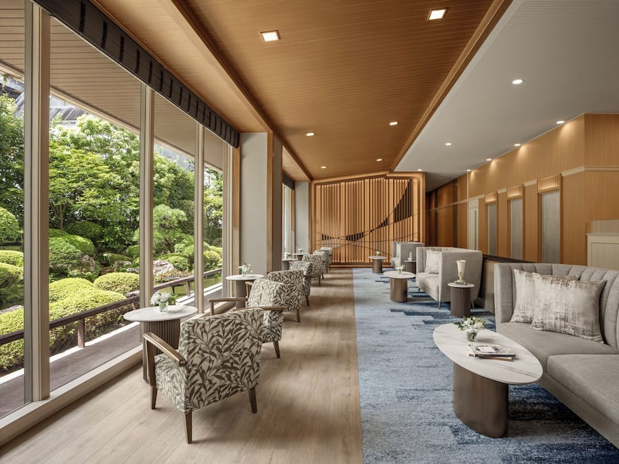 Um hall de hotel com um corredor longo, área de estar e vista para um jardim.