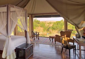 Um quarto com tenda, com uma cama, uma cadeira, uma mesa e vista para a paisagem.