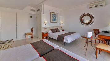 Quarto de hotel com duas camas, uma escrivaninha, uma cadeira, um guarda-roupa e um espelho fixado na parede.