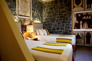 Quarto com duas camas, parede de pedra, mapa e mesa de cabeceira com abajur.
