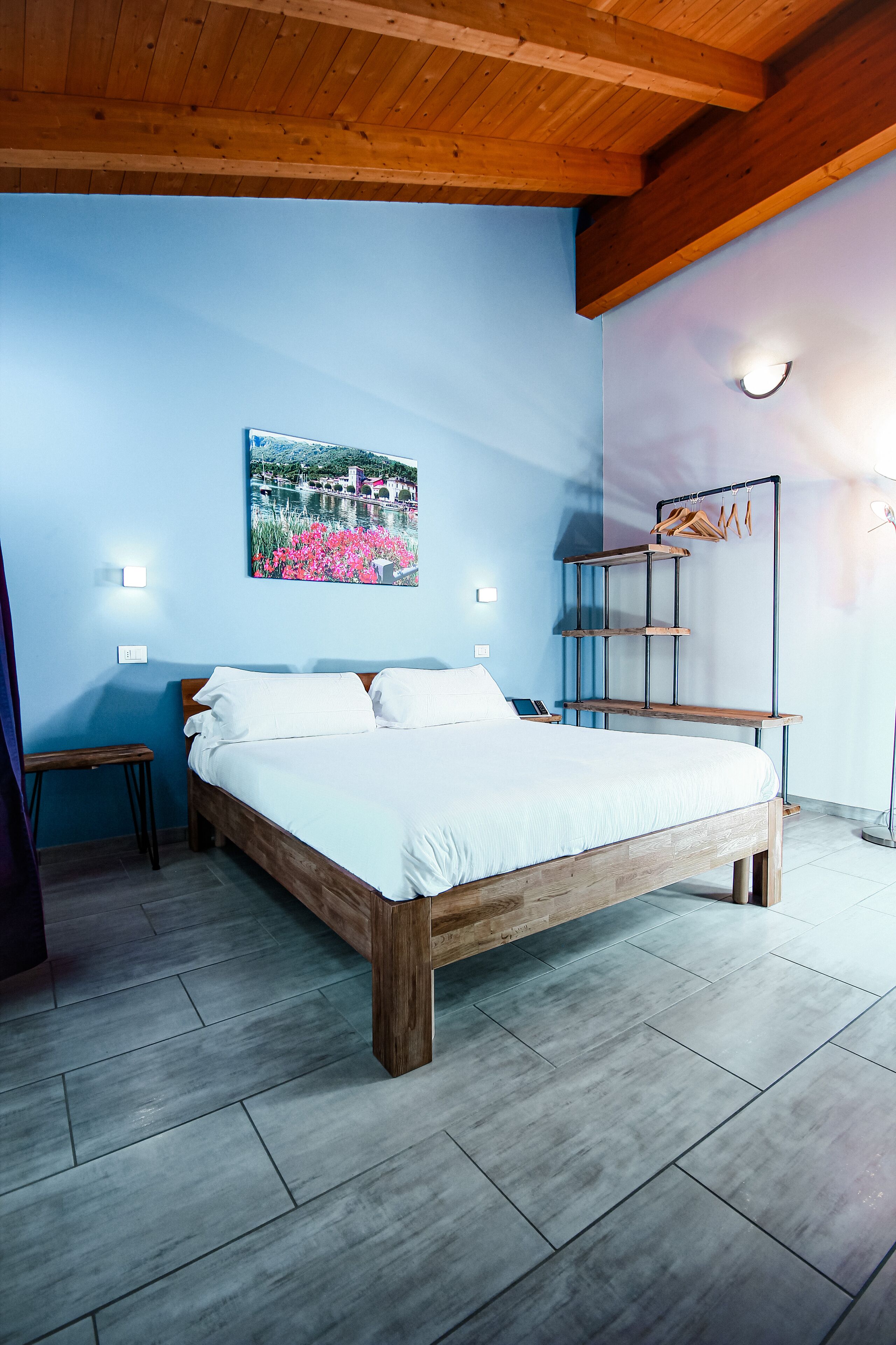 Quarto com cama de madeira, mesa de cabeceira, prateleira na parede e um quadro.