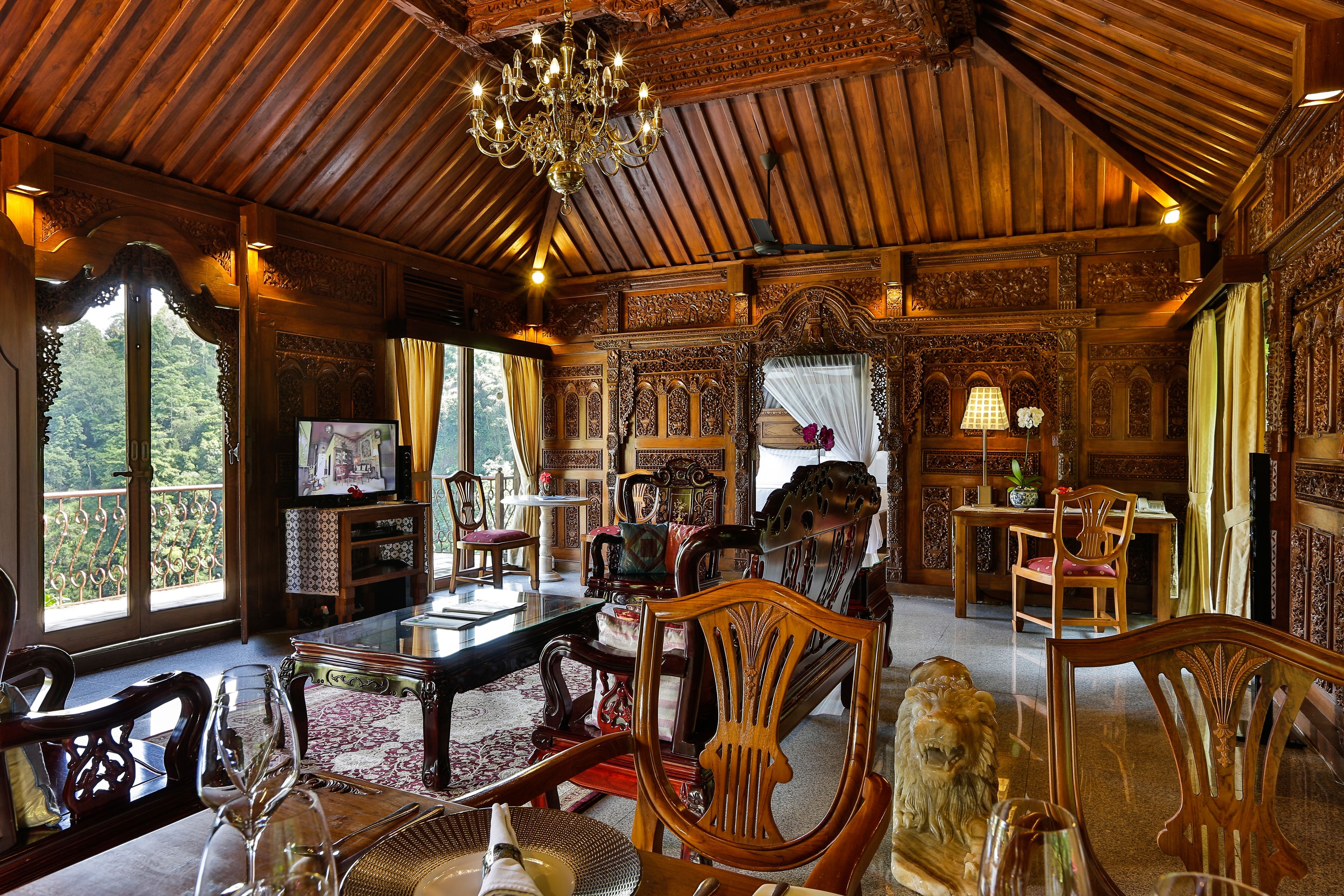 Quarto luxuoso com móveis de madeira ornamentados, um candelabro e uma grande janela com vista panorâmica.