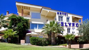 Um hotel com estrutura em dois andares, varandas e um jardim com palmeiras e arbustos.