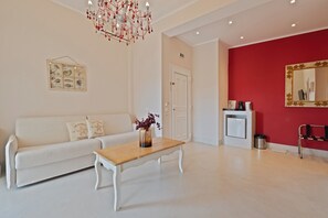 Um lobby de hotel moderno com um sofá branco, uma mesa de centro de madeira, uma parede de destaque vermelha, um pequeno frigorífico e um espelho.