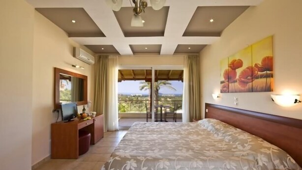 Quarto de hotel com cama, uma escrivaninha com computador, televisão e varanda com vista.