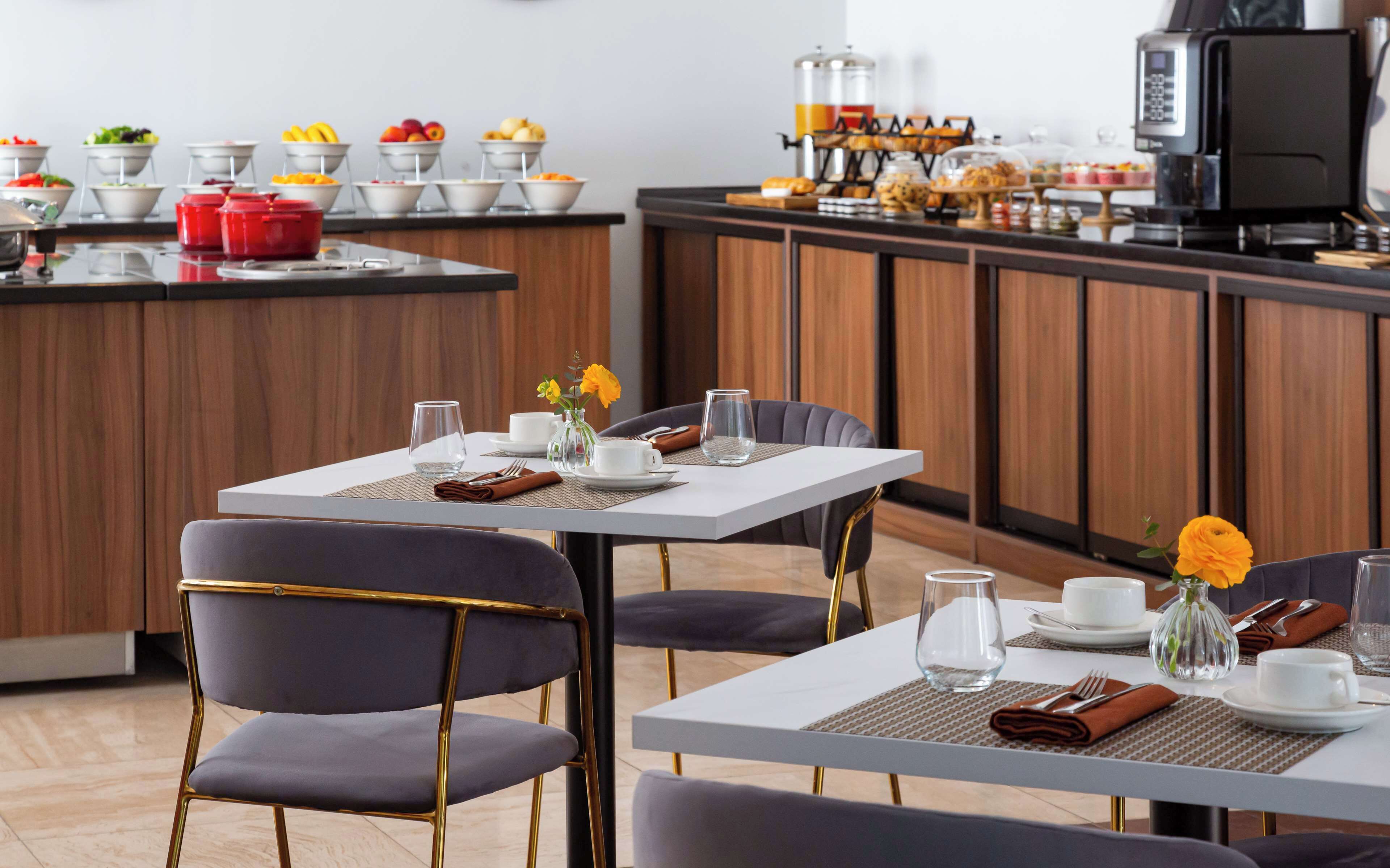 Uma área de refeições moderna com uma ilha central, onde se encontra uma máquina de café e tigelas de frutas.