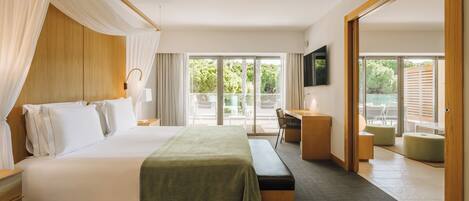 Quarto de hotel com cama, escrivaninha, televisão e varanda com área de estar ao ar livre.