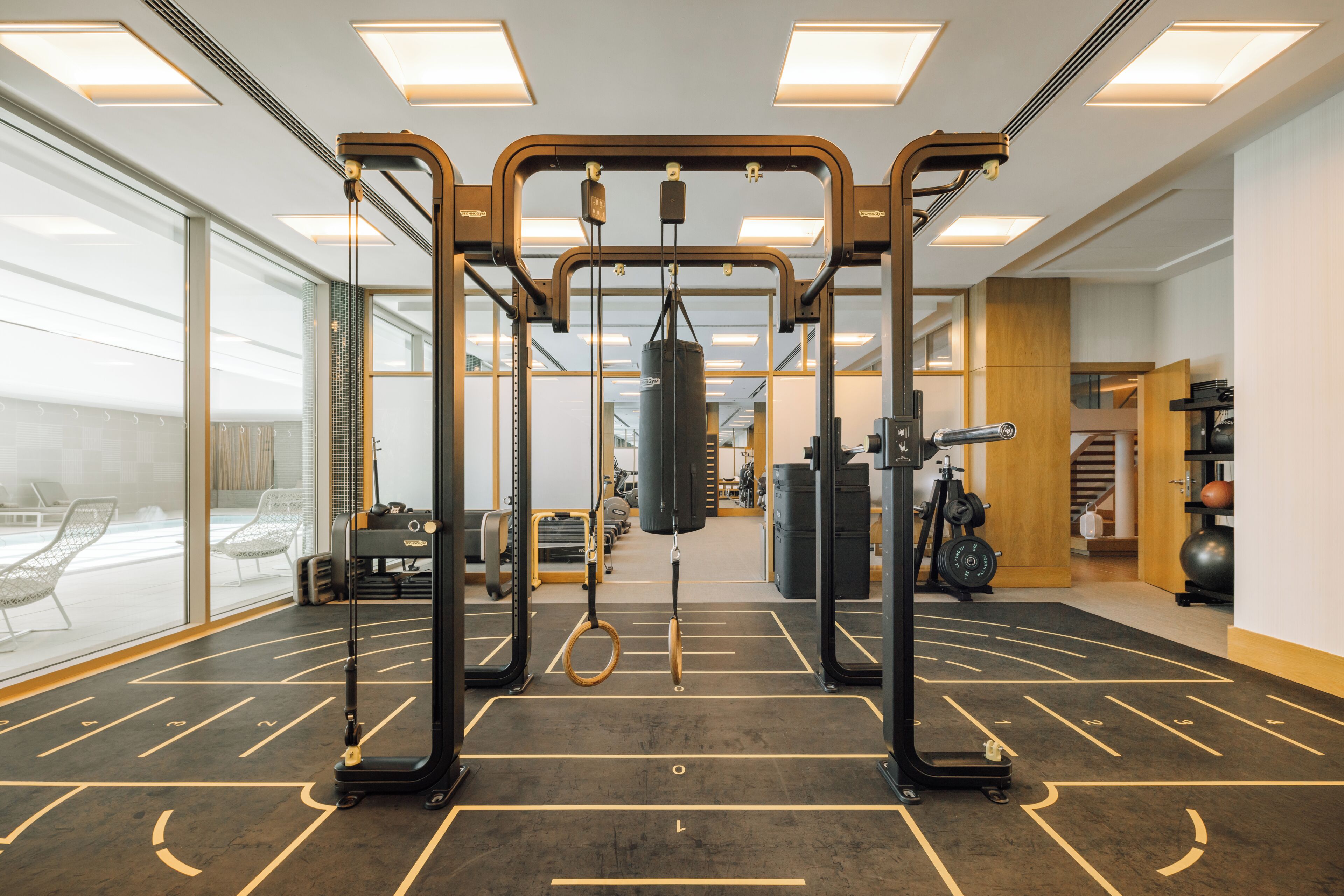 Uma academia com equipamentos de exercícios, um saco de pancadas e vista através de amplas janelas.