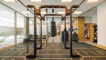 Uma academia com equipamentos de exercícios, um saco de pancadas e vista através de amplas janelas.