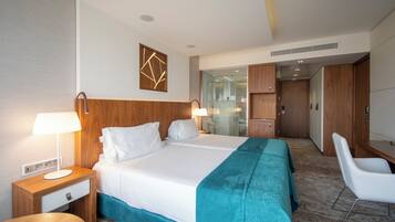 Quarto de hotel com cama, mesas de cabeceira, escrivaninha e uma cadeira.