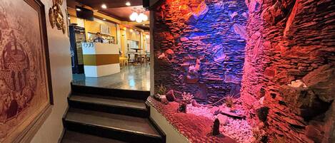 Uma escadaria leva a uma área de restaurante com uma parede de pedra e um pequeno elemento de água.