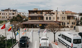 Hotel com um pátio central, várias bandeiras e estacionamento com diversos veículos.