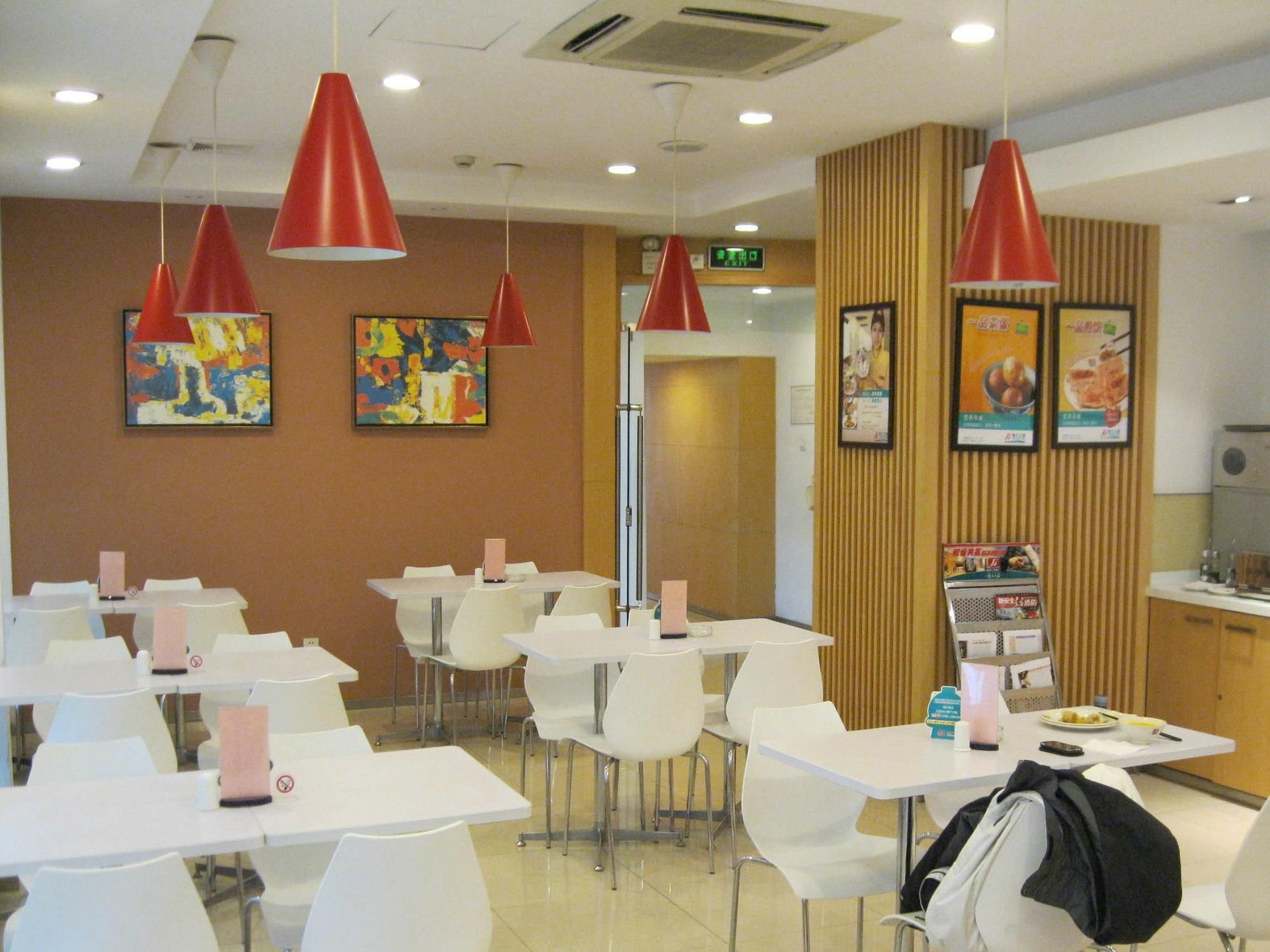 Uma sala de jantar com mesas e cadeiras, luminárias pendentes vermelhas e obras de arte nas paredes.