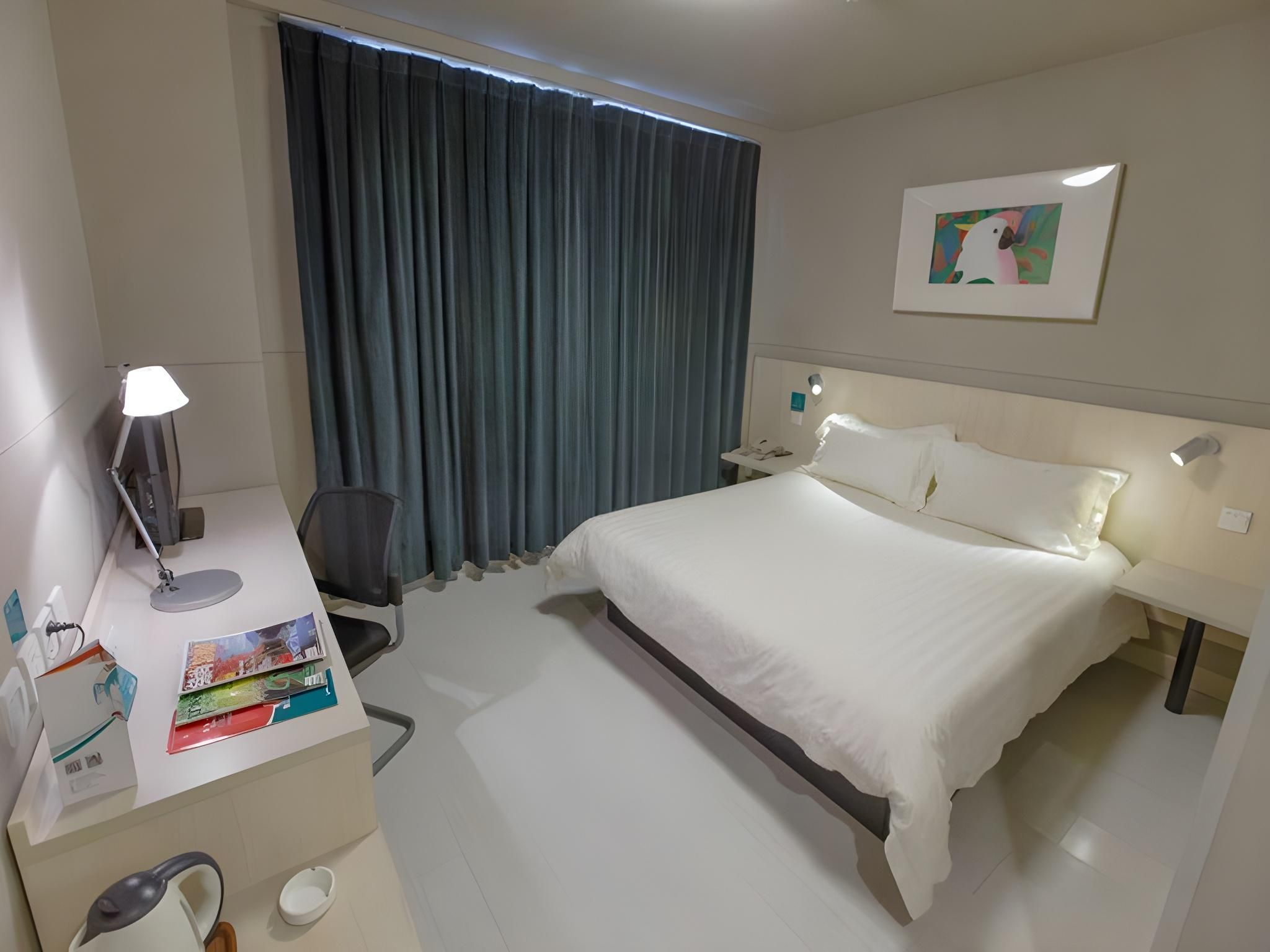 Quarto de hotel com cama, escrivaninha, cadeira, abajur e um quadro na parede.