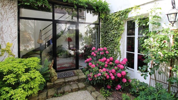 Um jardim com porta de vidro que dá para uma escadaria, rodeado por vegetação exuberante e plantas floridas.