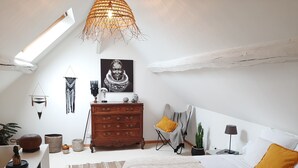 Quarto com cama, cômoda, cadeira, planta e luminária pendente.