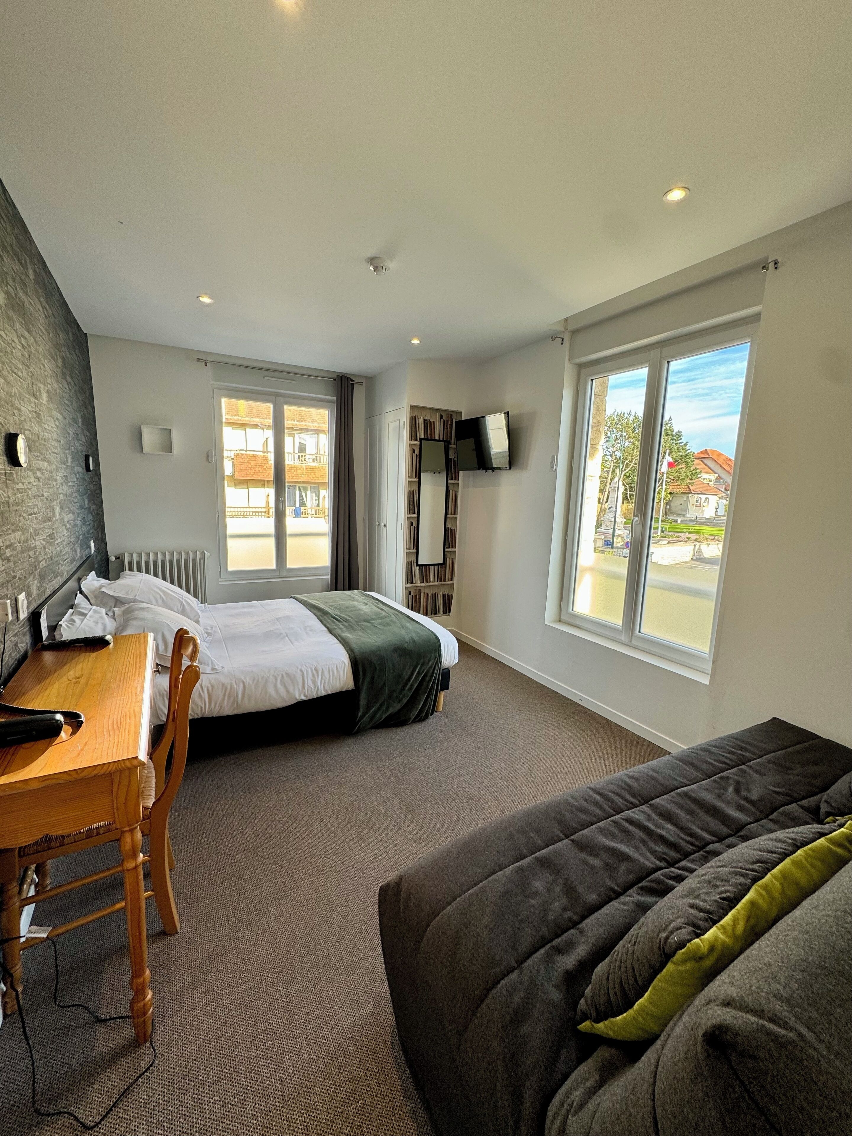 Quarto de hotel com uma cama, uma escrivaninha e uma cadeira. Há uma janela com vista para edifícios.