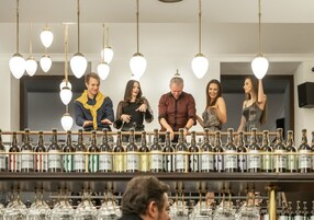 Um grupo de pessoas em uma área de bar, com várias garrafas e copos nas prateleiras.