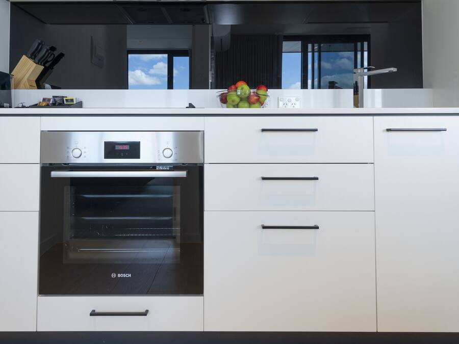 Cozinha moderna com forno Bosch, armários brancos e uma fruteira no balcão.