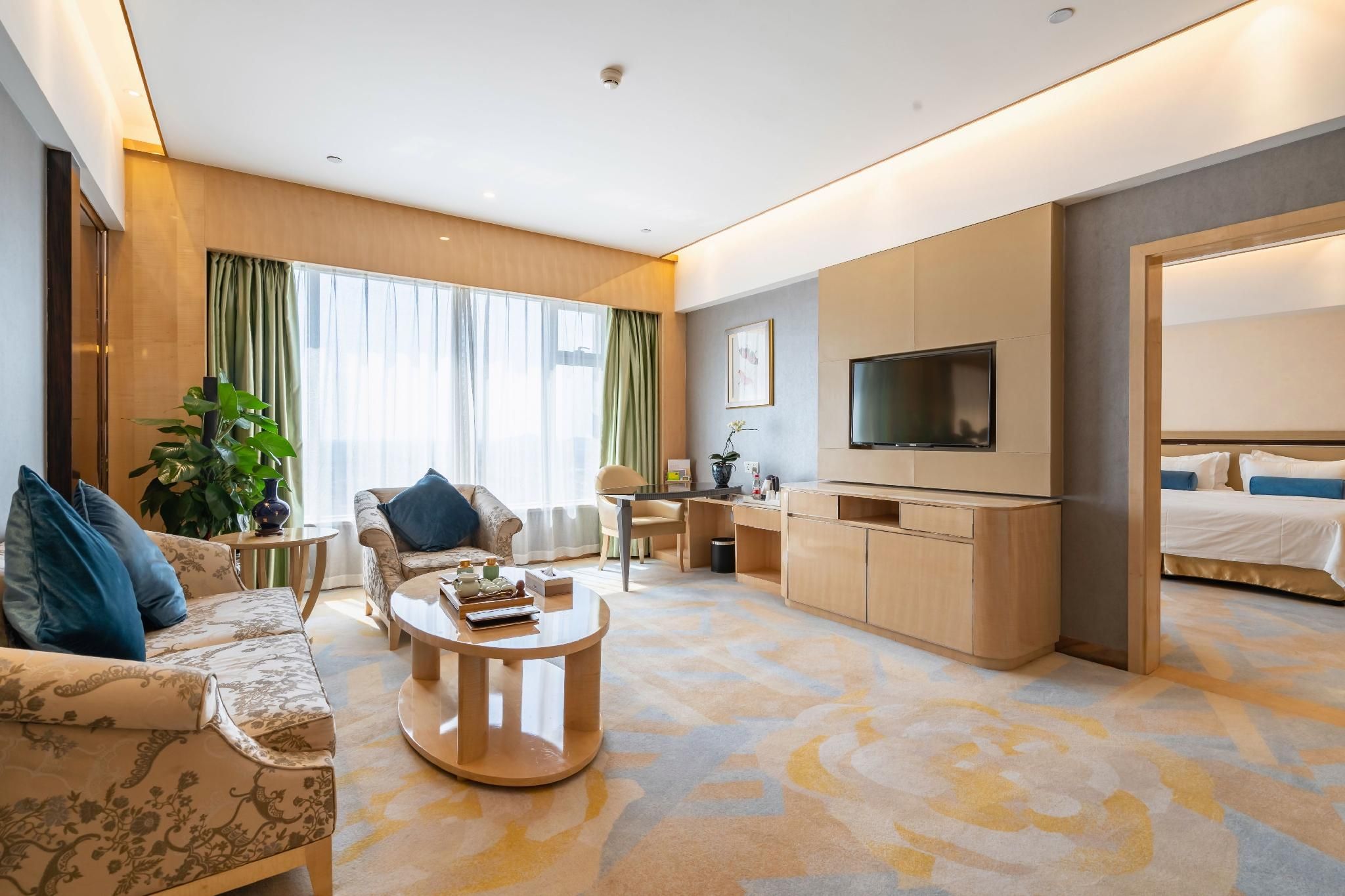 Quarto de hotel moderno com sofá, poltrona, mesa de centro, televisão e cama.