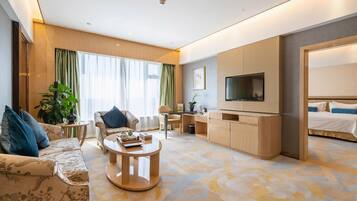 Quarto de hotel moderno com sofá, poltrona, mesa de centro, televisão e cama.