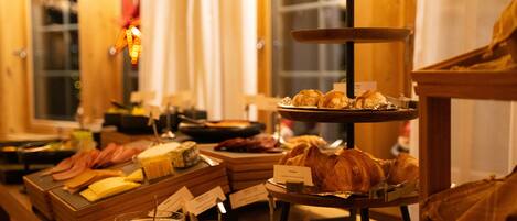 Buffet com diversos alimentos e bebidas, incluindo pastelaria, queijos e uma seleção de sumos.