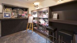 Uma área de recepção com balcão em madeira escura, tela digital e vitrine de vidro com diversos itens.