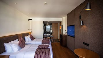 Quarto de hotel com duas camas, televisão, mesinha e espelho.