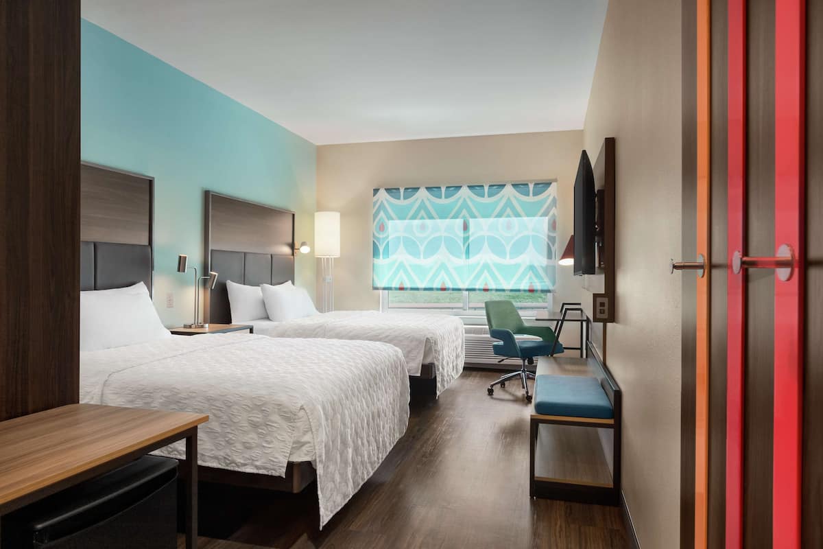 Quarto de hotel com duas camas, uma escrivaninha, uma cadeira, televisão e janela com vista decorada.