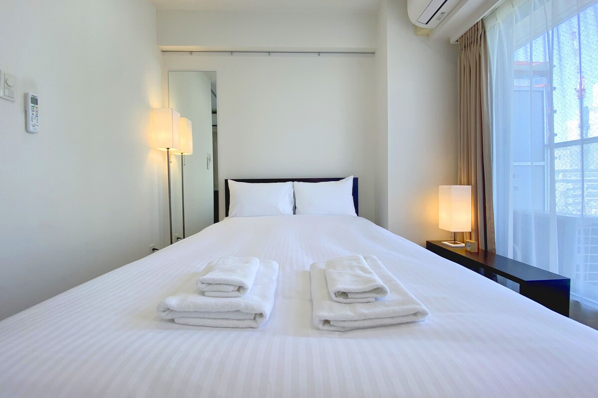 Quarto de hotel com uma cama grande, duas luminárias de cabeceira, mesa de apoio e janela com cortinas.