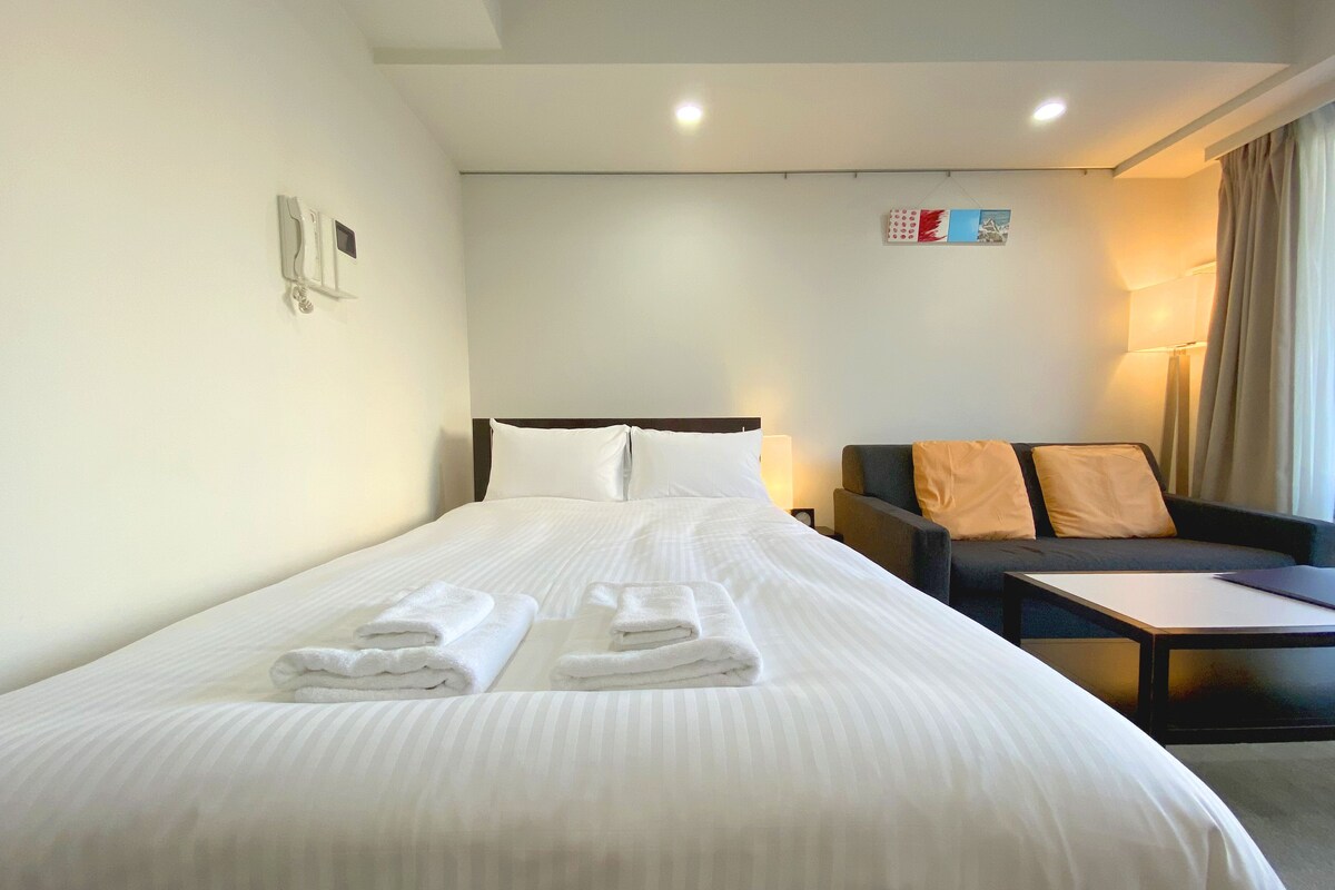 Quarto de hotel com uma cama grande, um sofá, uma mesa pequena e uma luminária.