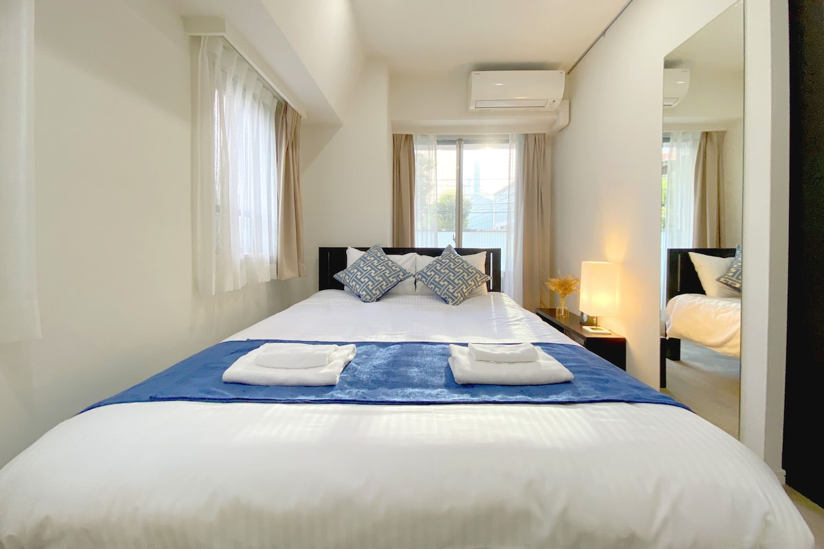 Quarto de hotel com uma cama grande, mesa de cabeceira com abajur, espelho e unidade de ar condicionado na parede.