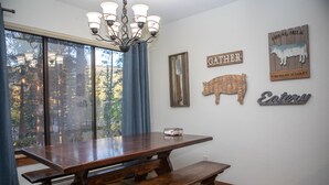 Uma sala de jantar com mesa e bancos de madeira, um candelabro e decorações nas paredes, incluindo uma vaca e as palavras "Gather" e "Eatery".