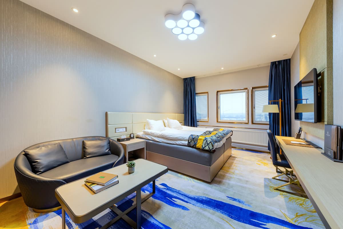 Quarto de hotel moderno com sofá, cama, escrivaninha e uma grande janela.