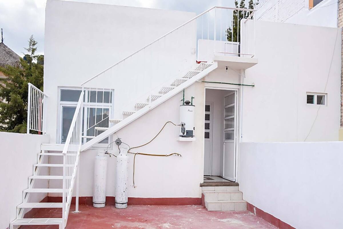 Um edifício branco com uma escadaria que leva a uma varanda, um aquecedor de água e uma pequena janela.