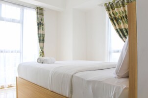 Cama bem arrumada com lençóis brancos, cabeceira de madeira e janela com cortinas leves.