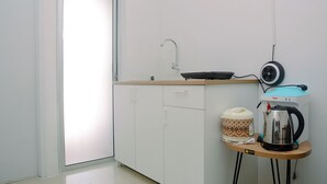 Cozinha com armários brancos, pia, cafeteira e chaleira sobre uma mesa pequena.