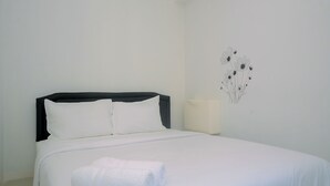Uma cama bem arrumada com lençóis brancos e uma toalha branca dobrada, um abajur e uma pintura floral na parede.